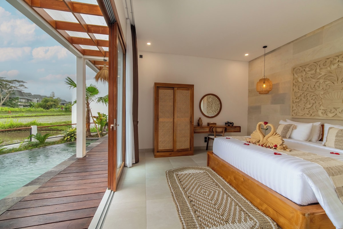 Quarto com cama de madeira, vista para um corpo d'água e varanda.