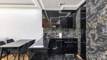 Cozinha moderna com bancadas pretas, forno embutido e painel de fundo em mármore.