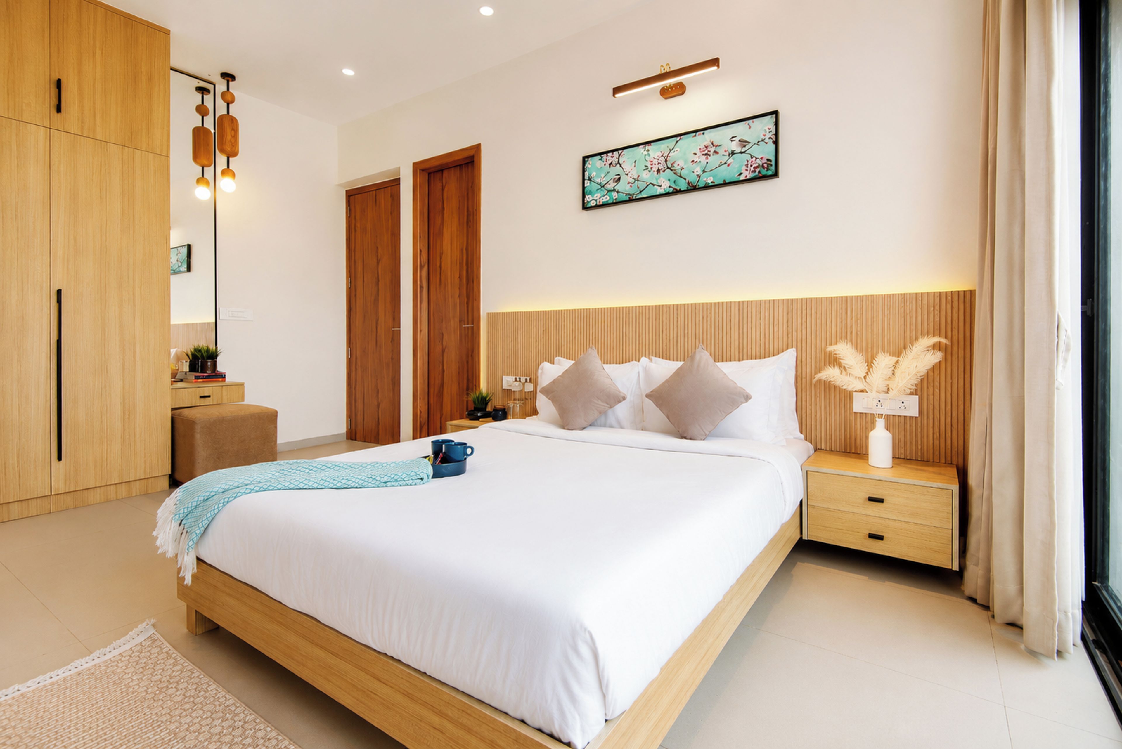 Um quarto moderno com uma cama grande, guarda-roupa de madeira, mesas de cabeceira e um criado-mudo com objetos decorativos.
