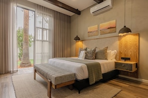 Quarto com uma cama grande, mesas de cabeceira, um banco e vista para o exterior.