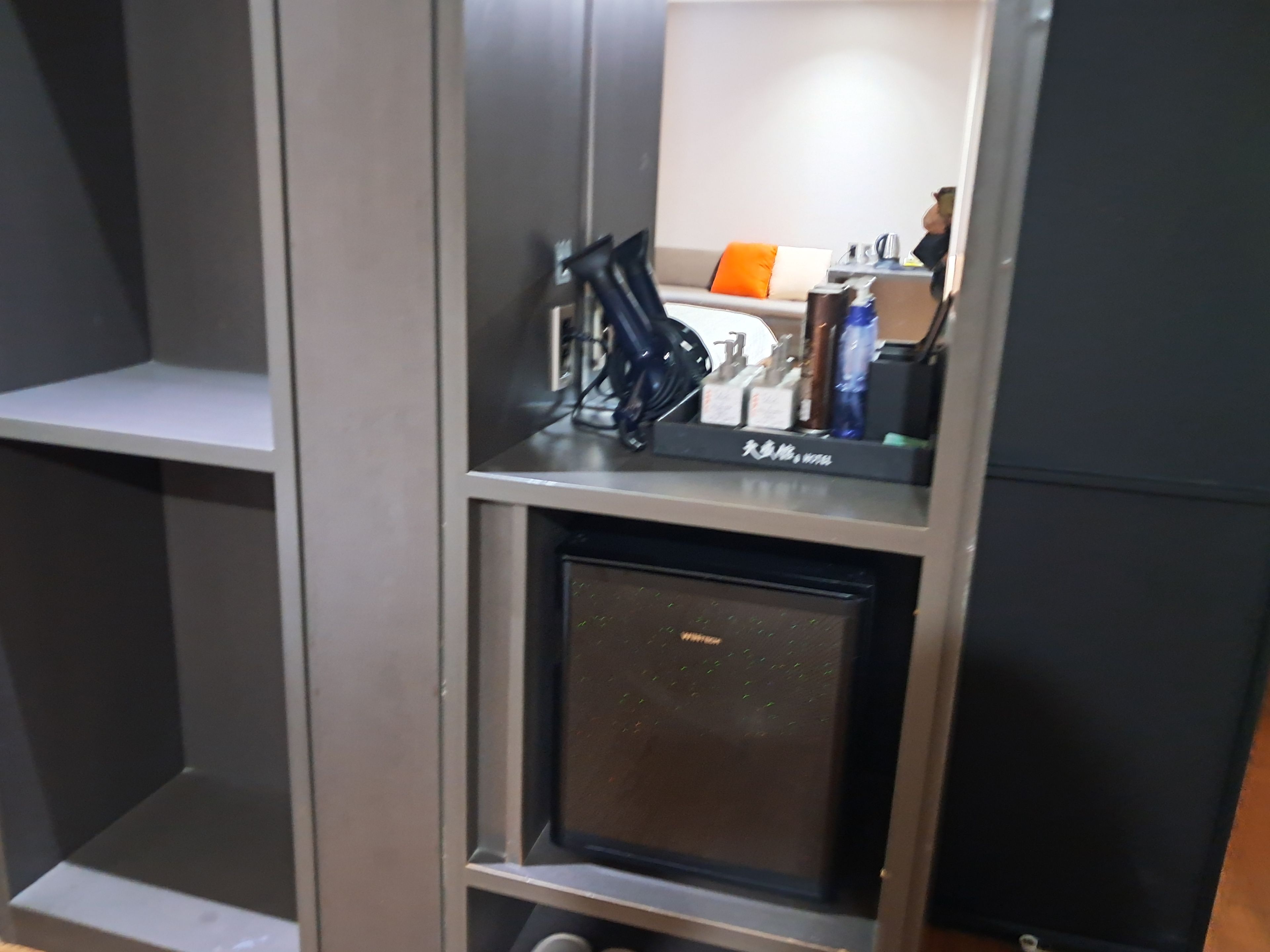 Quarto com geladeira embutida e prateleira com diversos objetos.