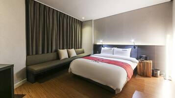 Quarto de hotel moderno com cama, sofá, mesa de cabeceira e abajur.