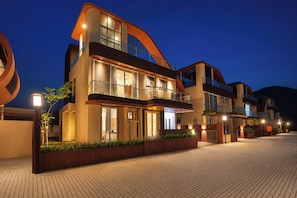 Um edifício residencial moderno de vários andares com uma arquitetura curva marcante, grandes janelas e uma entrada bem iluminada.