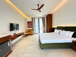 Quarto de hotel com cama, escrivaninha, cadeira, televisão e ventoinha no teto.