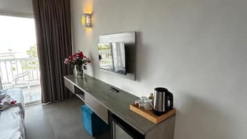 Quarto de hotel com cozinha compacta, cama, mesa pequena com um vaso de flores e vista para o exterior.