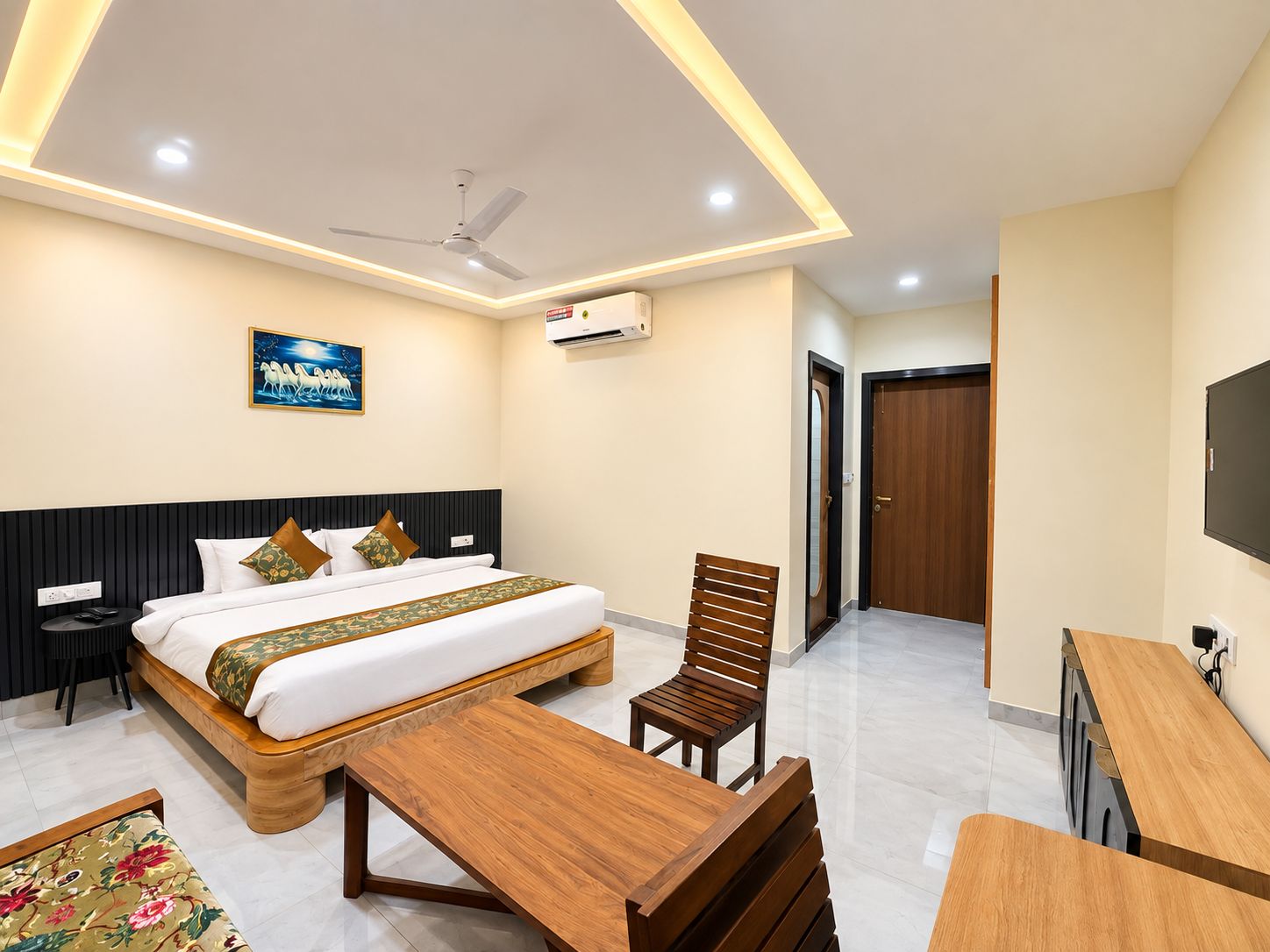 Quarto de hotel com cama, escrivaninha, cadeira, televisão e ventoinha no teto.