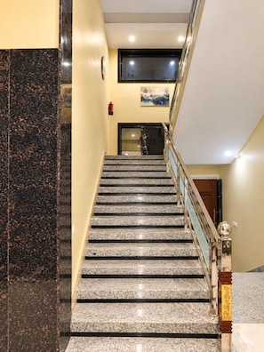 Uma escadaria com corrimão, um extintor de incêndio na parede e um quadro sobre a porta.