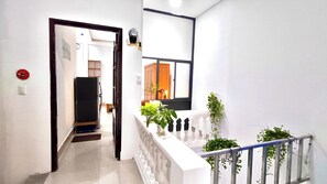 Um corredor com corrimão branco, uma porta que dá para um quarto e uma janela com vista para outro quarto.