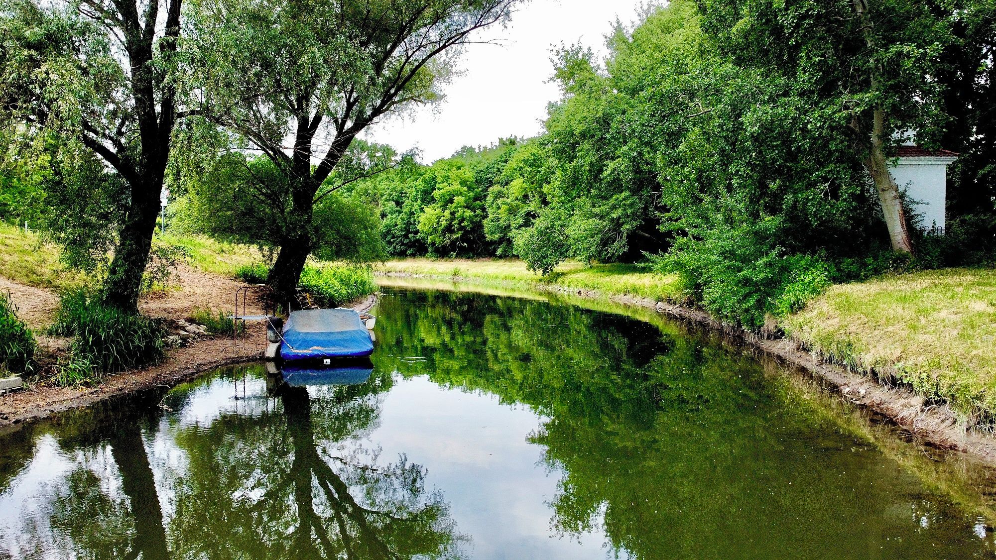 Um rio calmo com um barco atracado na margem esquerda, rodeado por vegetação exuberante e árvores.