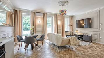 Uma sala de estar ampla com uma TV grande, uma área de jantar com mesa de vidro e um espaço de estar aconchegante com tapete estampado.