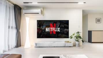 Uma sala de estar moderna com uma grande televisão de tela plana na parede, um console branco, um sofá de couro marrom e um abajur de chão alto.