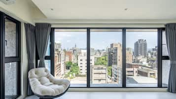 Quarto moderno com uma grande janela, uma poltrona estofada e vista para a paisagem urbana.