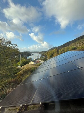Painéis solares no telhado, um lago e uma encosta arborizada.