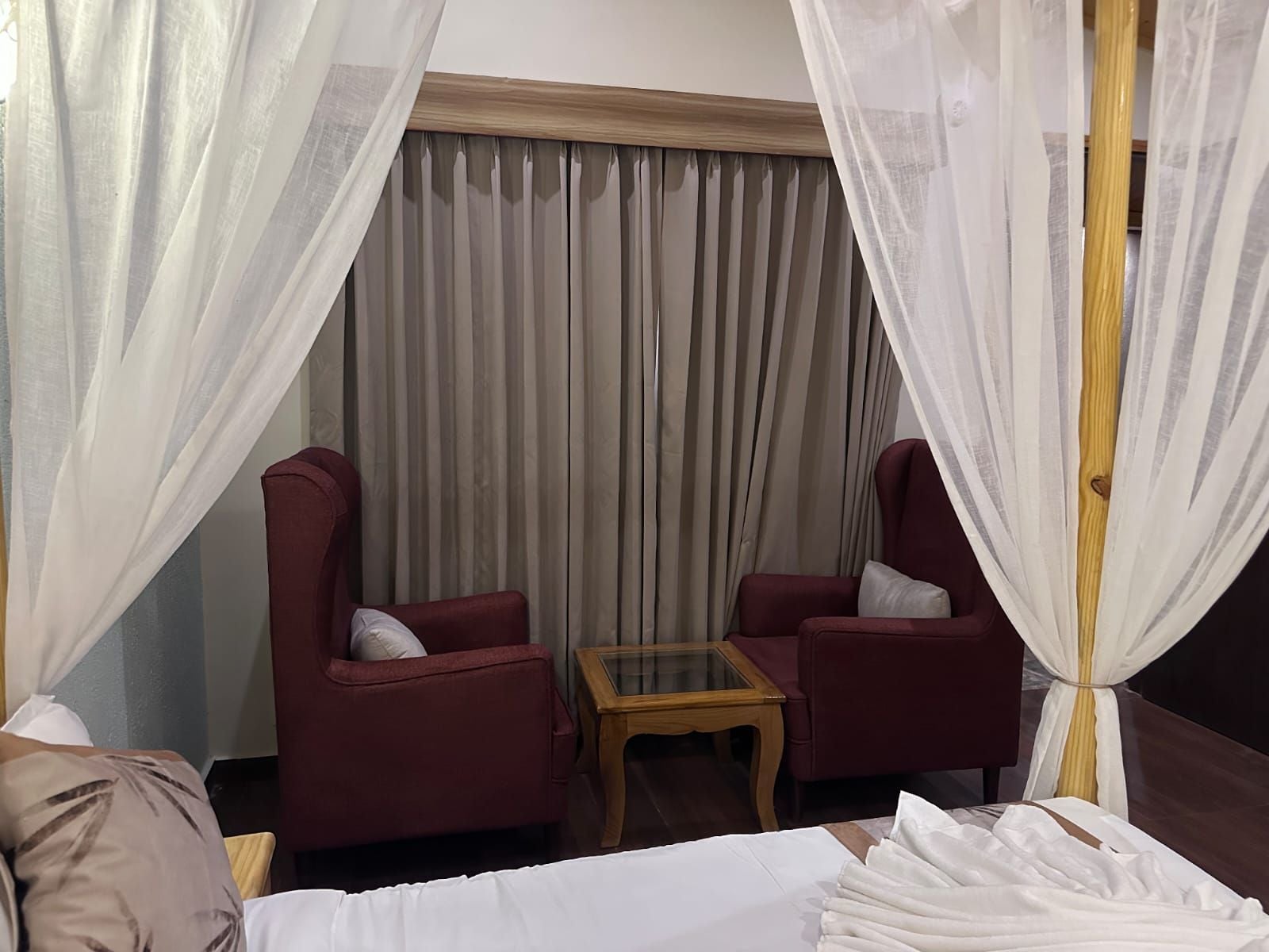 Quarto com duas poltronas, uma mesinha e uma cama com roupa de cama branca.