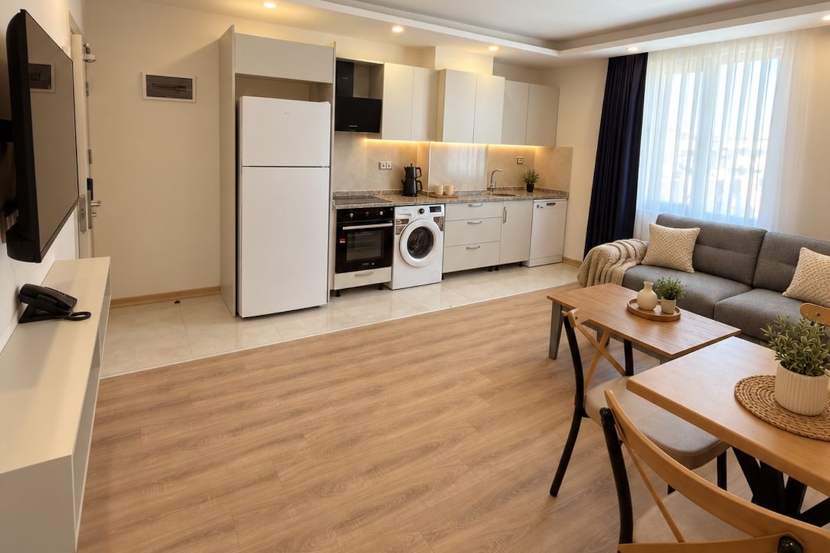 Cozinha moderna equipada com frigorífico, forno e máquina de lavar roupa. Possui um espaço de refeições com mesa e cadeiras.