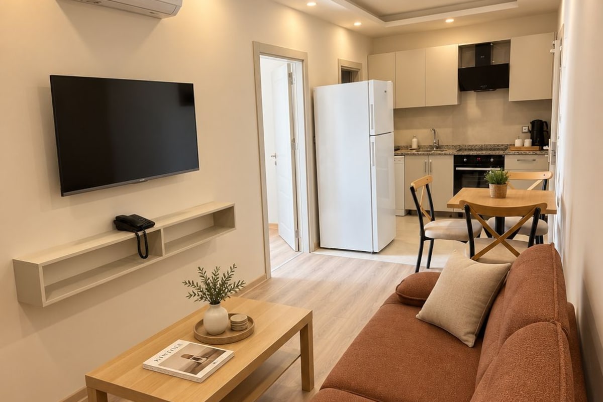 Uma sala de estar moderna com sofá, mesa de centro, TV de tela plana e cozinha ao fundo.