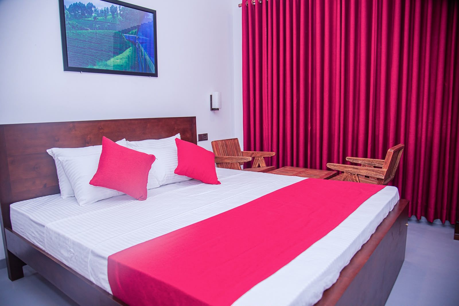 Quarto de hotel com uma cama grande, cortinas vermelhas, cabeceira de madeira e um quadro na parede.