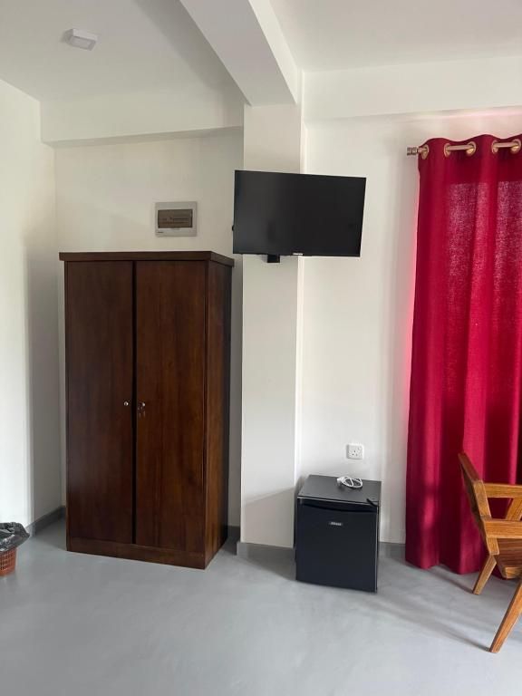 Quarto com guarda-roupa, um armário preto, televisão na parede e cortina vermelha.