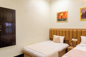 Quarto de hotel com guarda-roupa de madeira, cama com cabeceira e duas pinturas nas paredes.