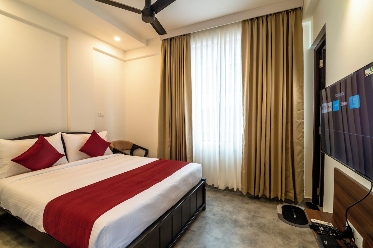 Quarto de hotel com cama, escrivaninha com computador, televisão e cortinas.