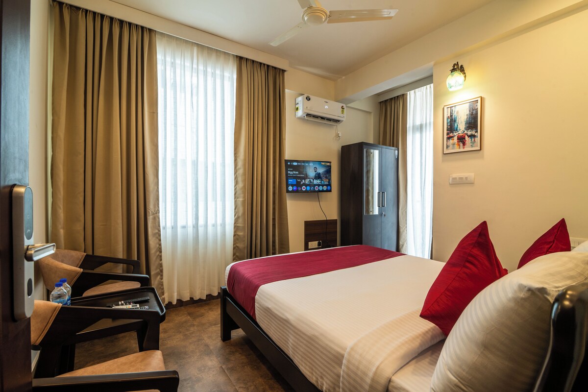 Quarto de hotel com cama, escrivaninha, cadeira, televisão e ar condicionado.
