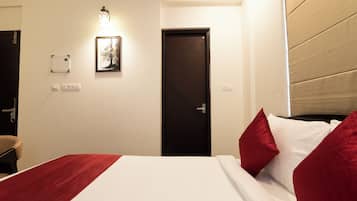 Quarto de hotel com cama, porta, luminária na parede e tomada.