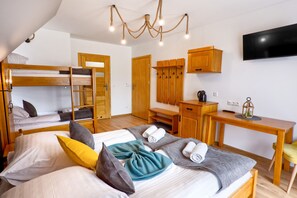 Quarto com beliches, escrivaninha, cadeira, televisão e cozinha compacta.