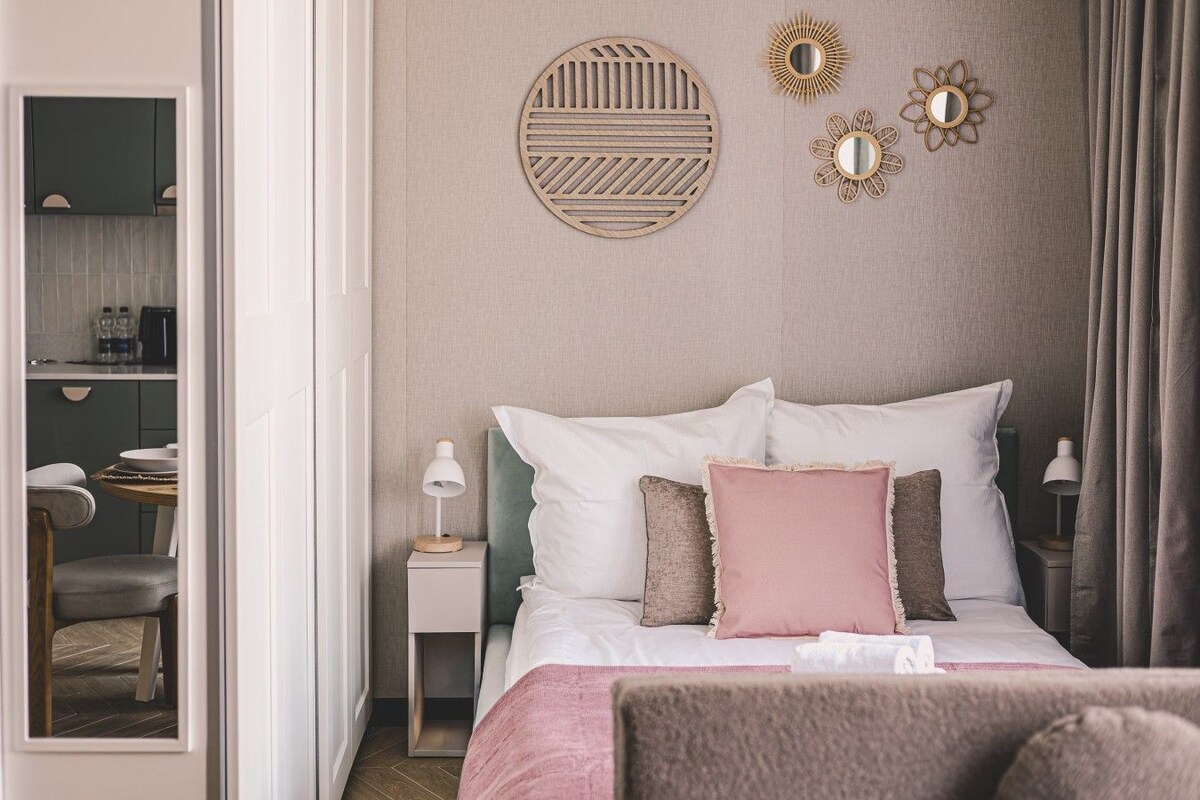 Quarto com cama, mesas de cabeceira, espelho e vista para uma área de refeições.