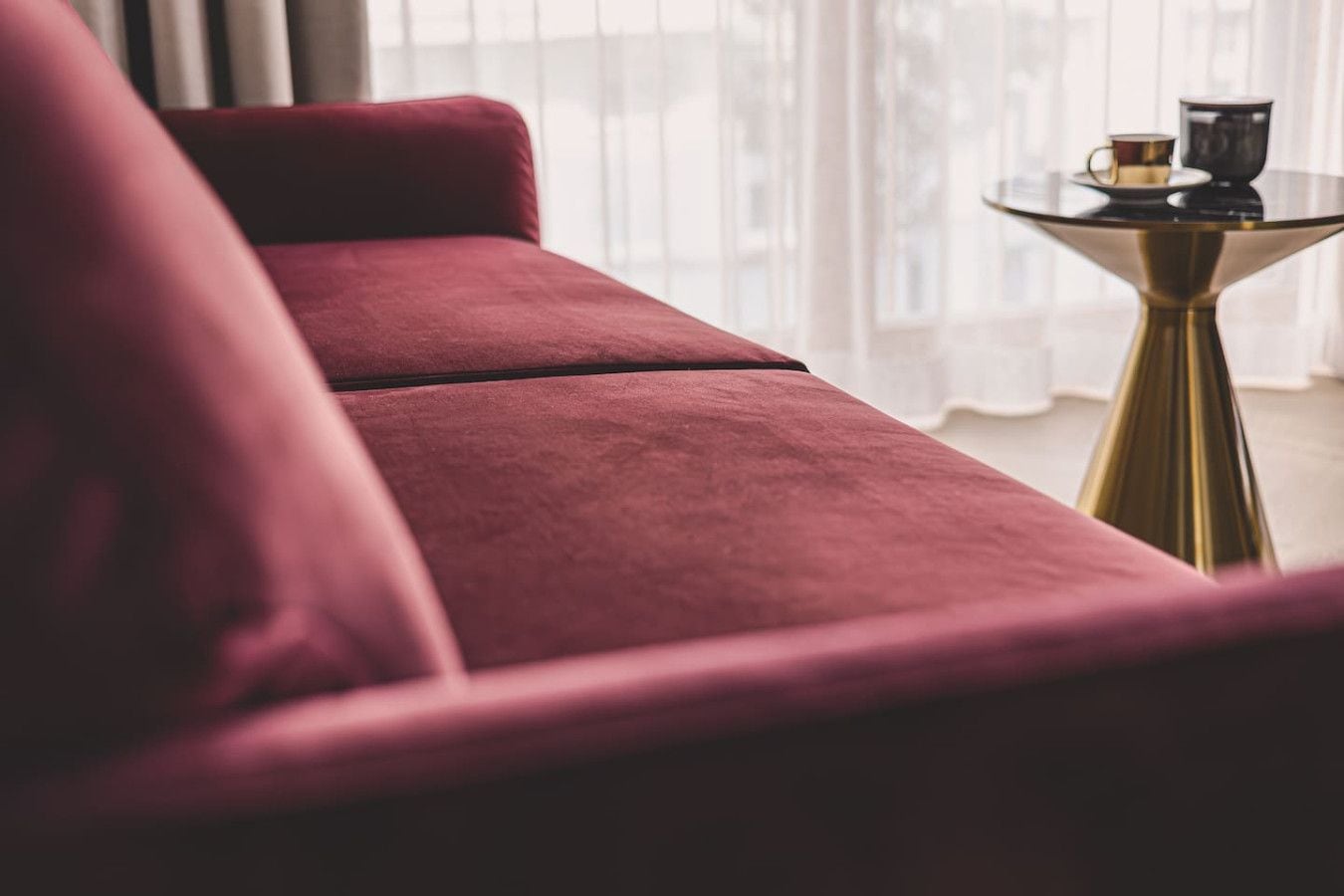 Um sofá vermelho em um quarto com uma pequena mesa redonda e uma xícara.