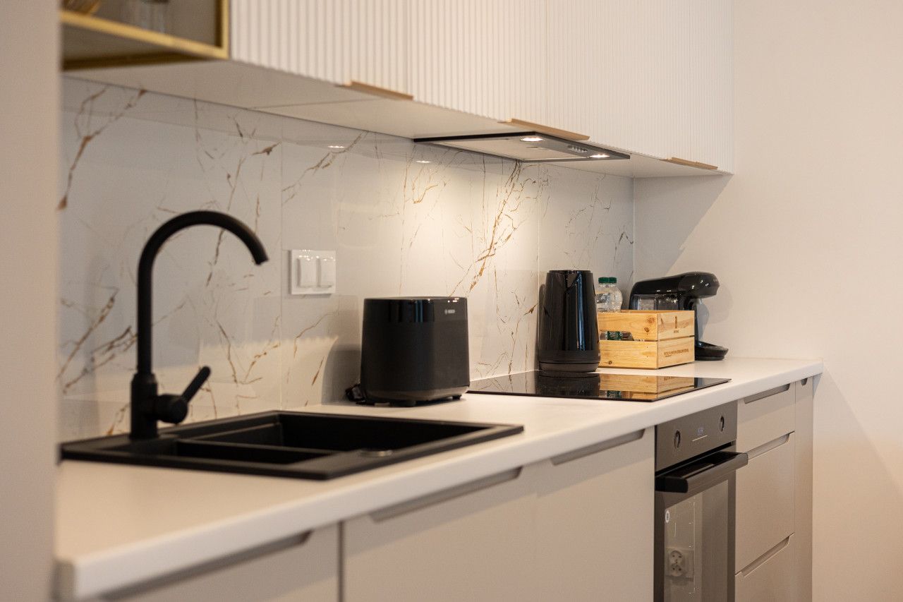 Cozinha moderna com bancada branca, torneira preta, cafeteira e embalagem de cápsulas de café.