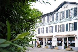 Um edifício de dois andares com fachada tradicional, apresentando uma varanda com plantas em vasos e uma placa indicando um restaurante ou café.