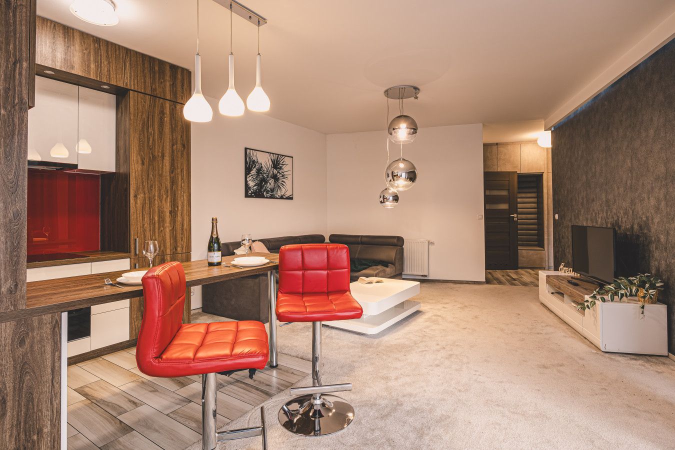 Uma sala de estar moderna com área de jantar, sofá, televisão e cozinha com armário de madeira e uma cadeira vermelha.
