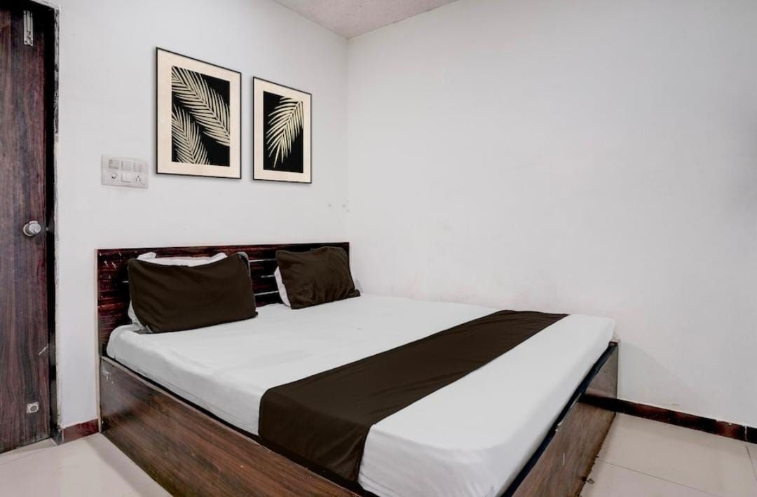 Cama de solteiro com cabeceira de madeira, roupa de cama branca e detalhes em tons de castanho. Há duas molduras com padrões de folhas na parede.