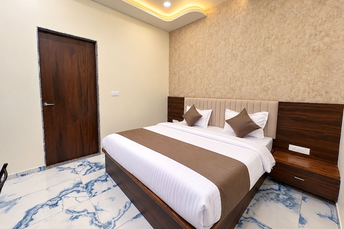 Quarto de hotel com uma cama grande, cabeceira de madeira, piso com padrão de mármore e uma porta.