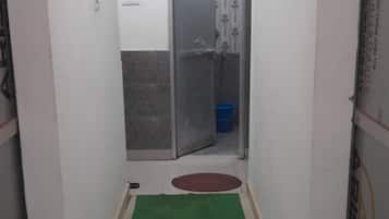 Um corredor estreito com carpete verde que leva a uma porta com painel de vidro.