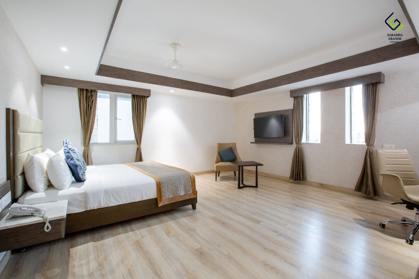 Quarto de hotel com cama, poltrona, televisão e escrivaninha.