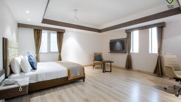 Quarto de hotel com cama, poltrona, televisão e escrivaninha.
