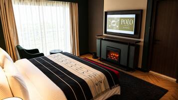 Quarto de hotel com cama, lareira, televisão e janela com cortinas.