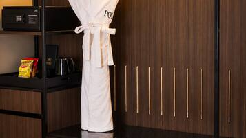 Quarto de hotel com armário contendo roupão branco, máquina de café e minibarra.