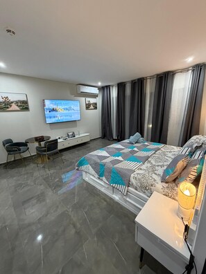 Quarto moderno com cama, televisão, escrivaninha e cadeira.