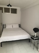 Quarto com cama, mesa de cabeceira, abajur e janela.