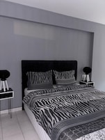 Um quarto moderno com colcha estampada em zebra, cabeceira preta e duas mesas de cabeceira com abajures redondos pretos.