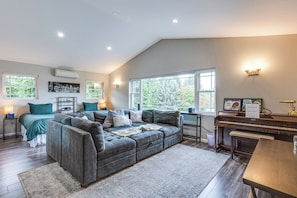 Uma sala de estar moderna com um sofá modular, um piano e janelas amplas com vista para árvores.