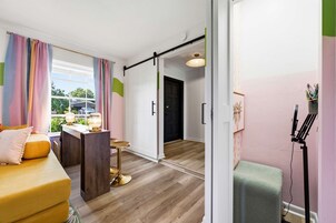 Sala de estar moderna com sofá, mesa pequena e cadeira. Uma porta deslizante dá acesso a outro cômodo.