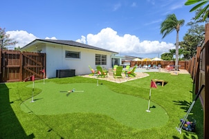 Um quintal com piscina, cadeiras verdes e uma casa pequena.