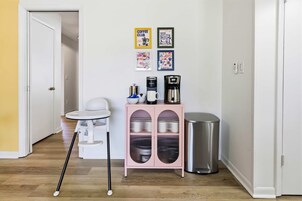 Cozinha compacta com cafeteira, lixeira e armário com arte temática de café.
