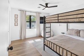 Quarto com beliche, ventilador no teto, janela com cortinas e tapete no chão.