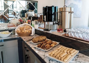 Buffet de café da manhã com diversos pães, bolos e uma estação de café.