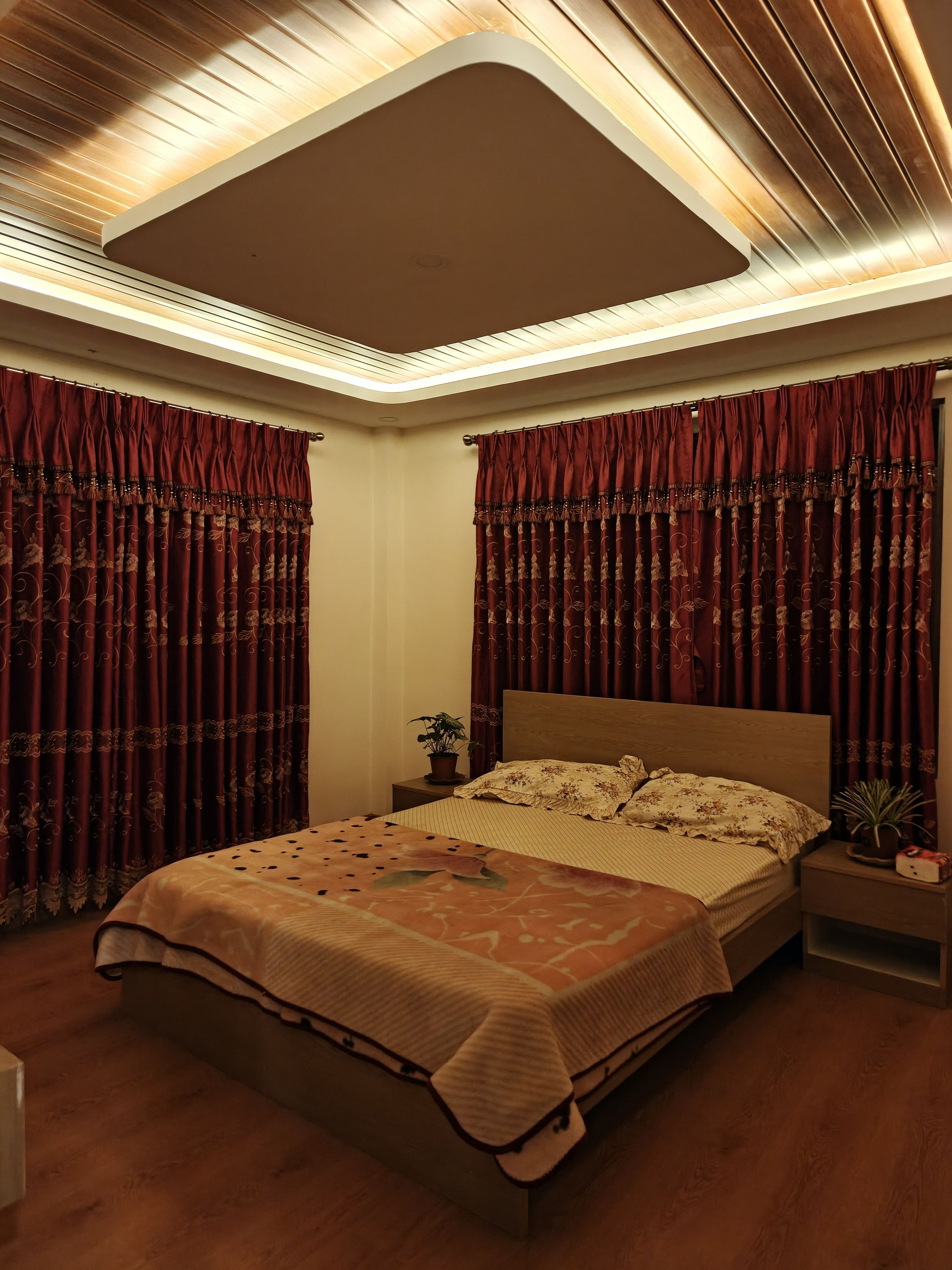 Quarto com cama grande, duas mesas de cabeceira, um criado-mudo, luminária no teto e um vaso com planta.
