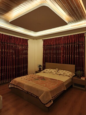 Quarto com cama grande, duas mesas de cabeceira, um criado-mudo, luminária no teto e um vaso com planta.